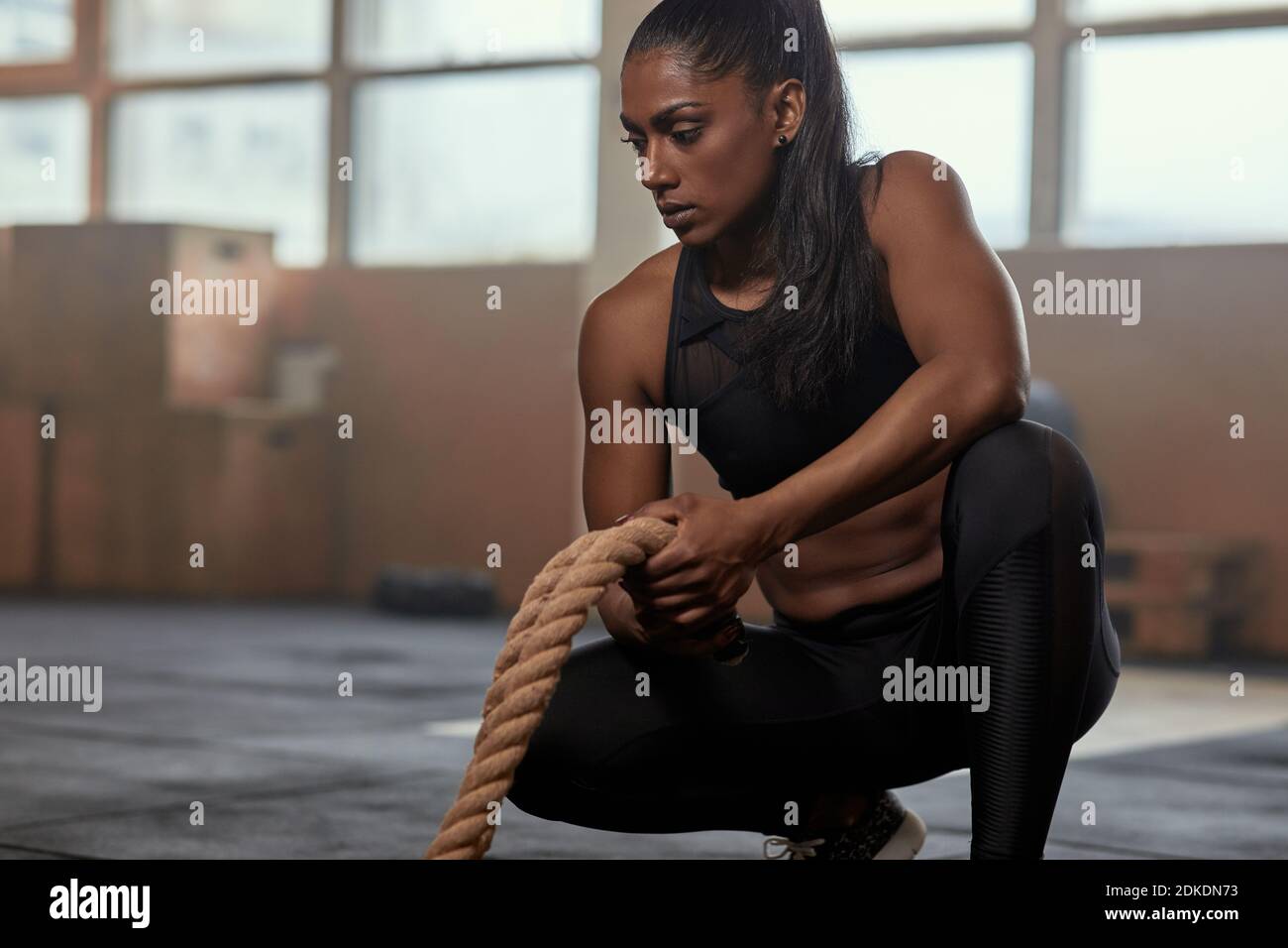 Fit young Indian woman in sportswear taking a break from a battle rope ...