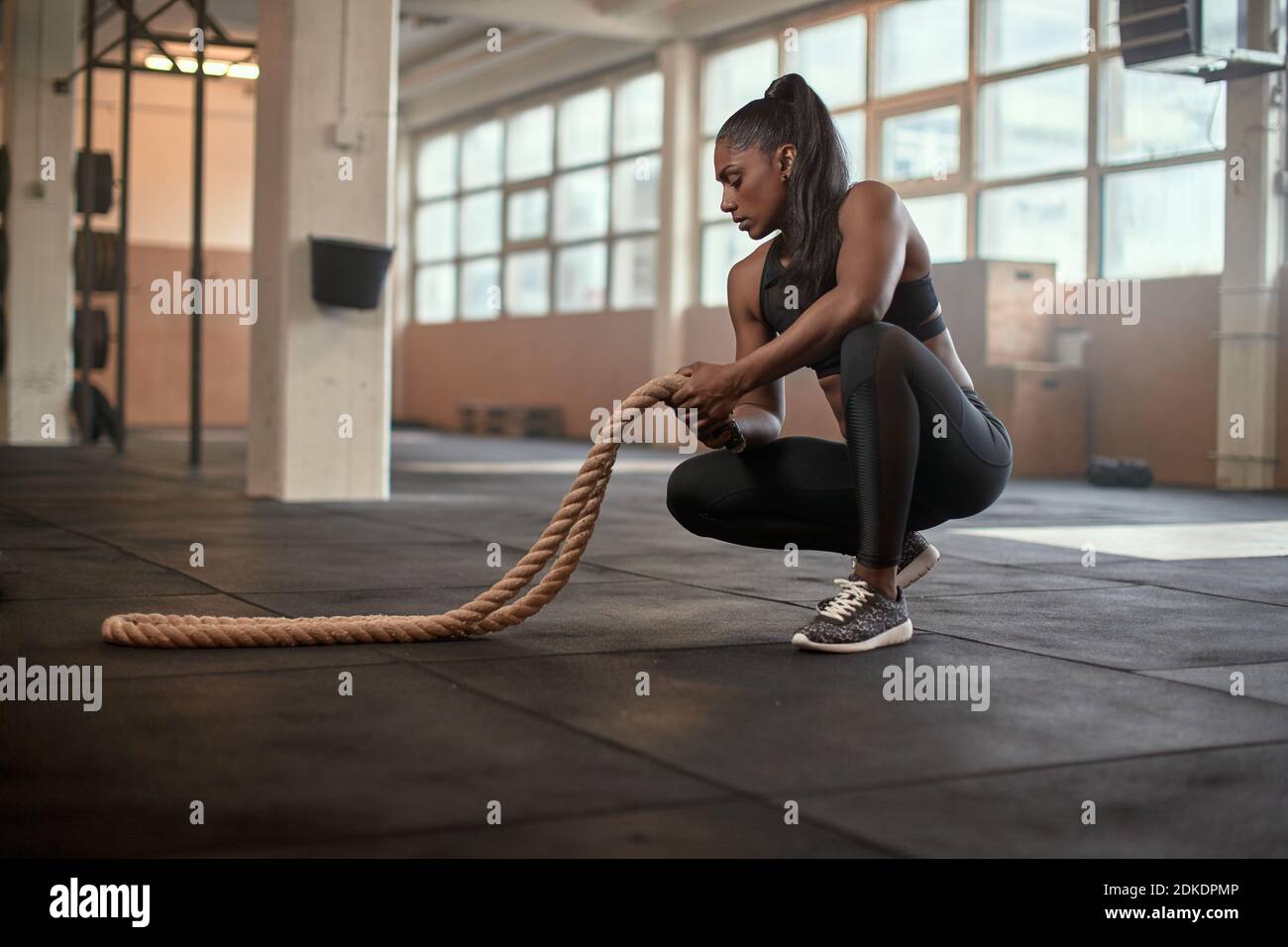 Fit young Indian woman in sportswear holding a battle rope while ...