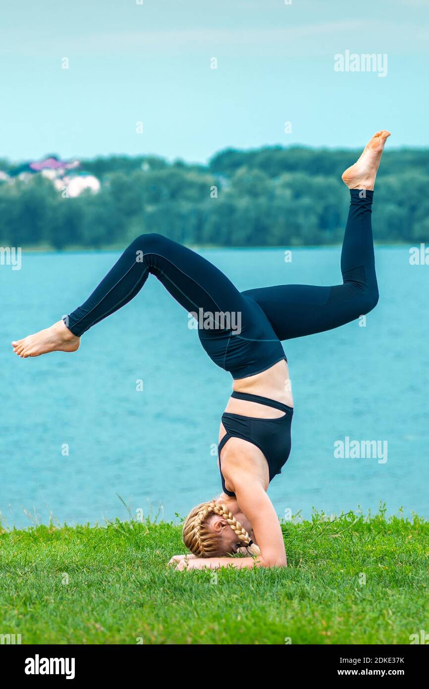 A woman does handstand exercises on the grass near the lake. Yoga ...