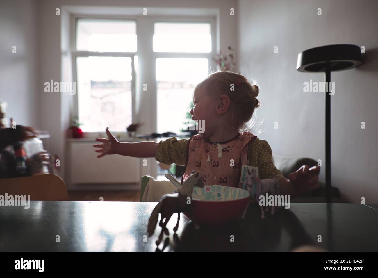 Baby girl reaching out hand and crying in front of food bowl. Medium ...