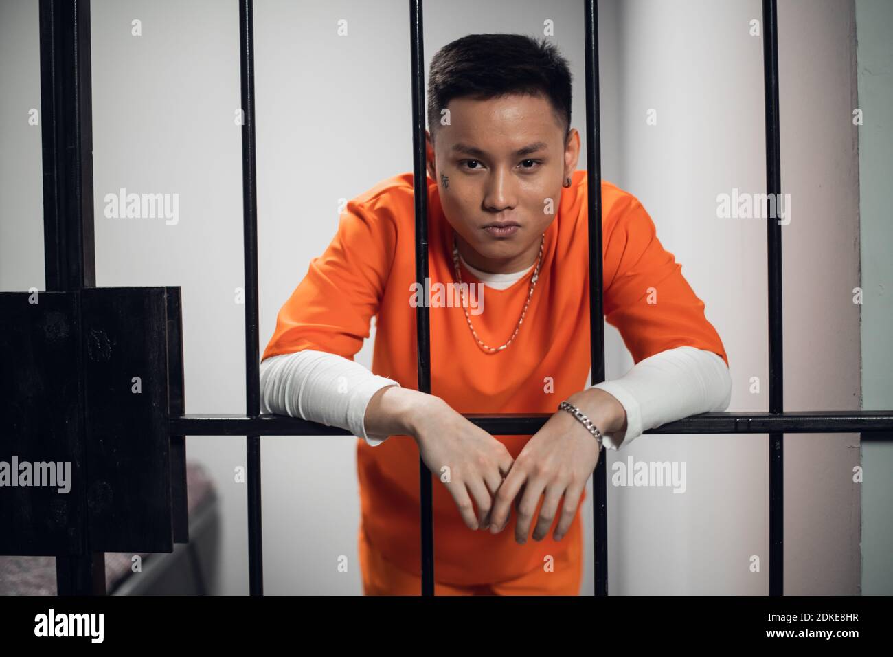 A young asian criminal poses for a photo against the bars in his cell ...