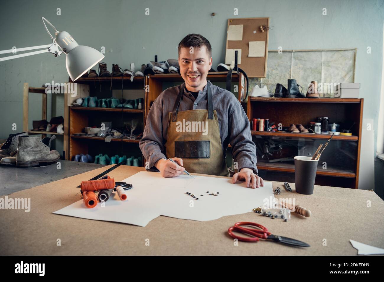 A young shoemaker makes a drawing for a pattern for leather shoes on a ...