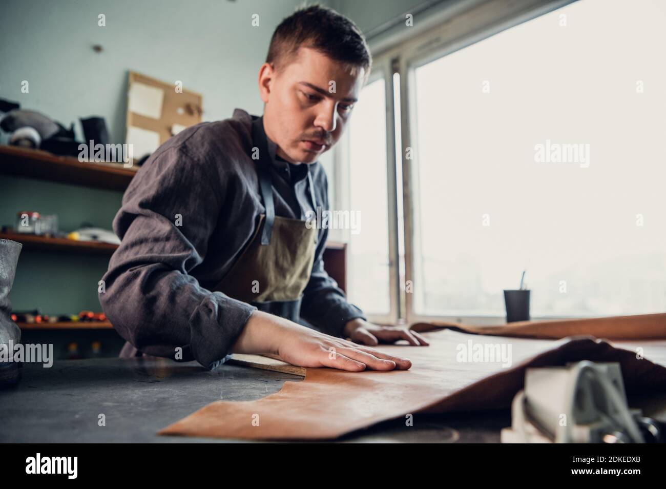A young shoemaker starts manufacturing shoes, lays out a roll of ...
