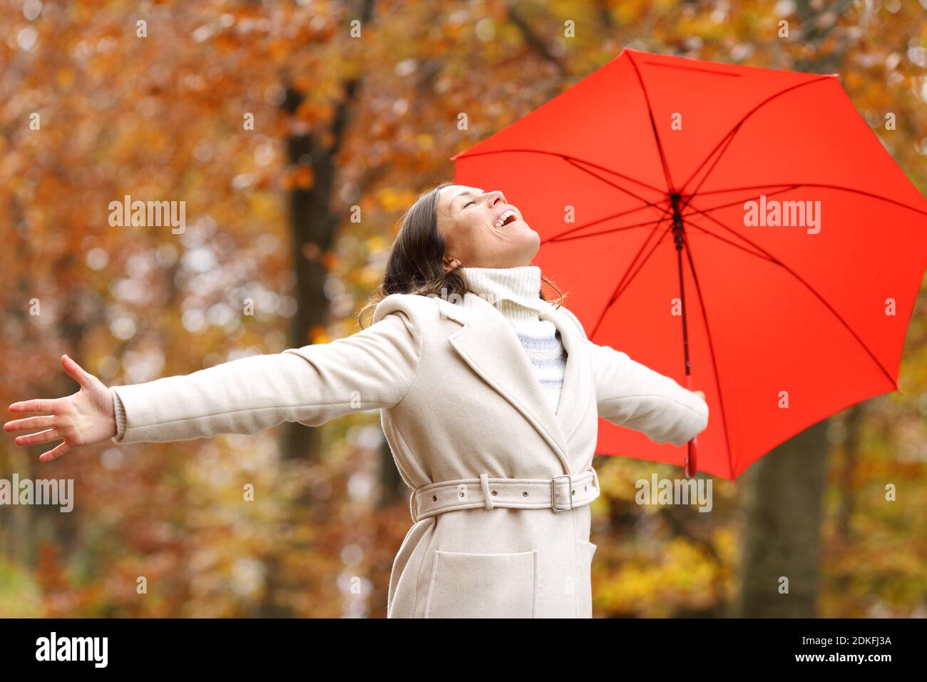 Happy fashion adult woman with umbrella celebrating autumn stretching ...