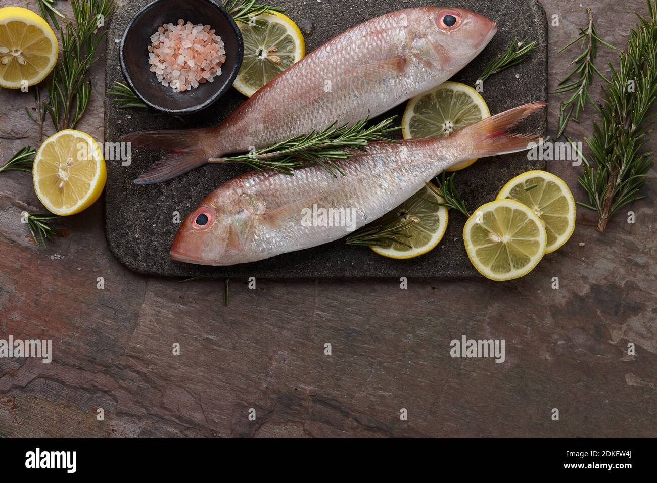Raw red mullet fish with lemons and herbs on stone background, copy ...