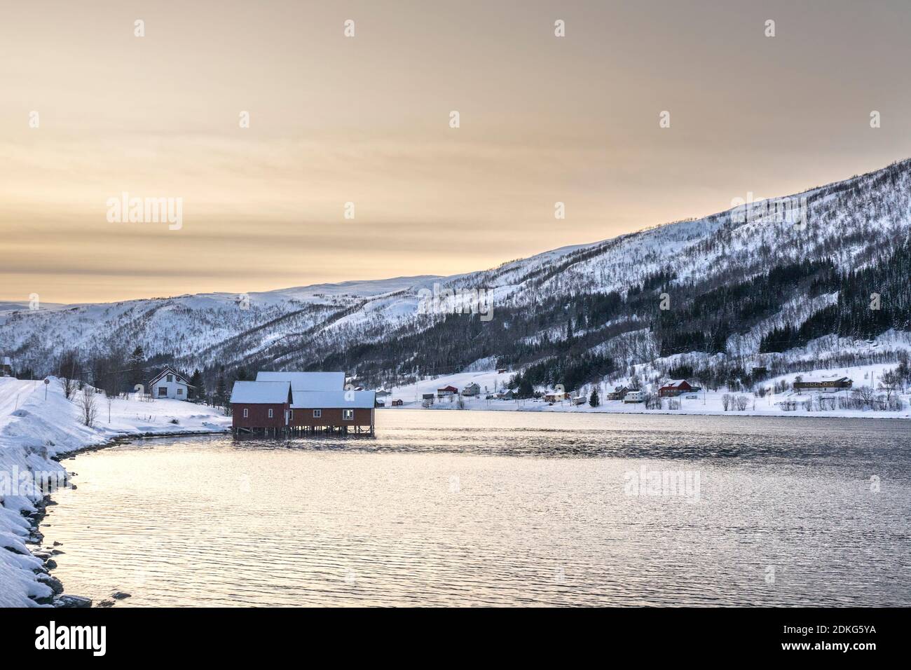 Red wooden house in the wintry, snow-covered landscape by the fjord in ...