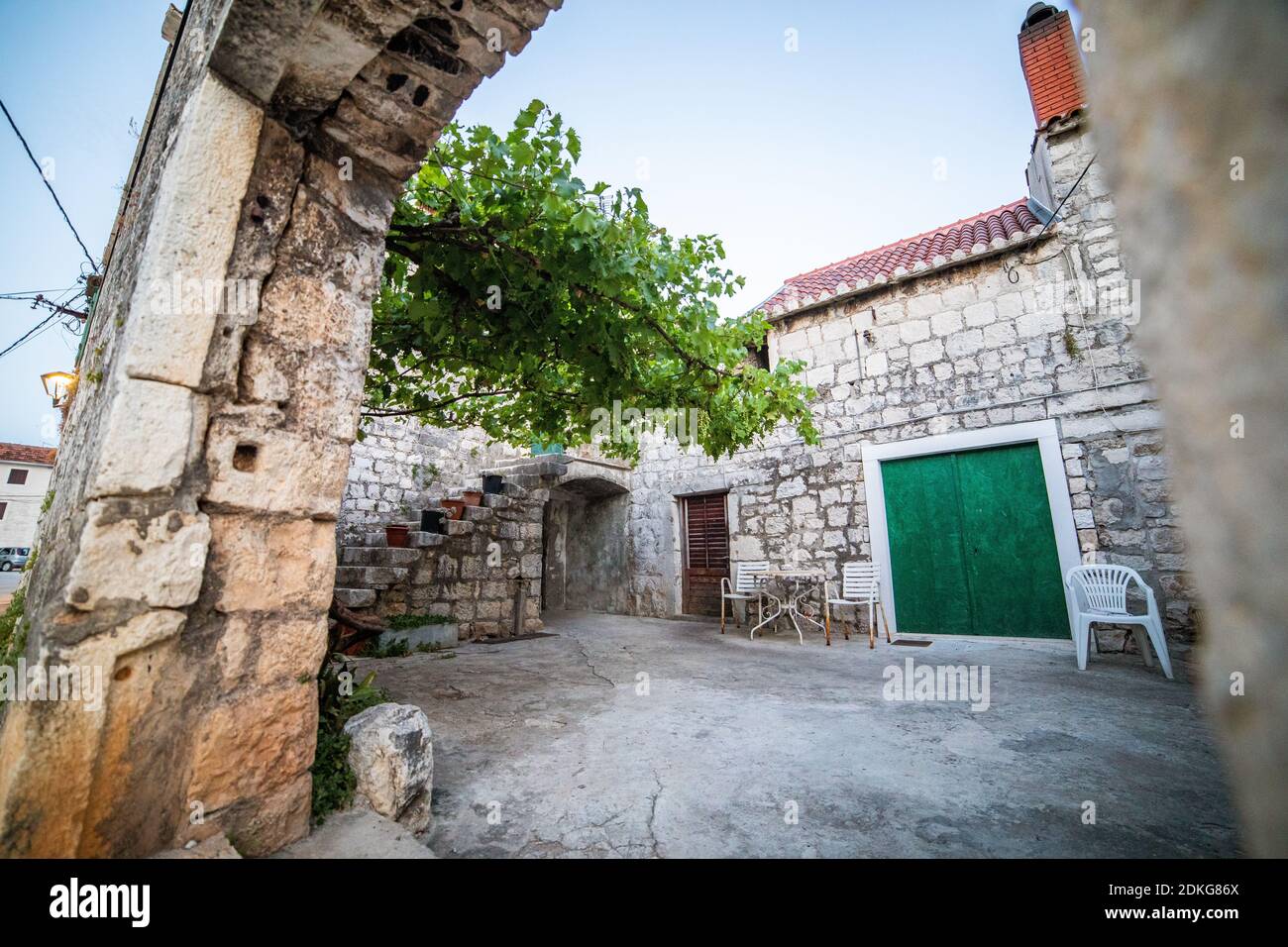 Typical Croatian courtyard with a tree and stone walls. Seating and a ...