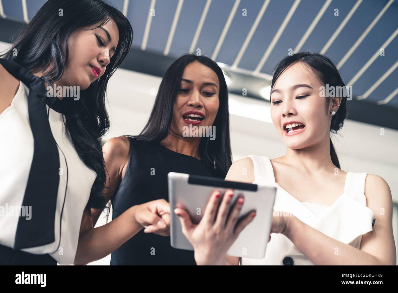 Three Asian women friends having conversation while looking at tablet ...