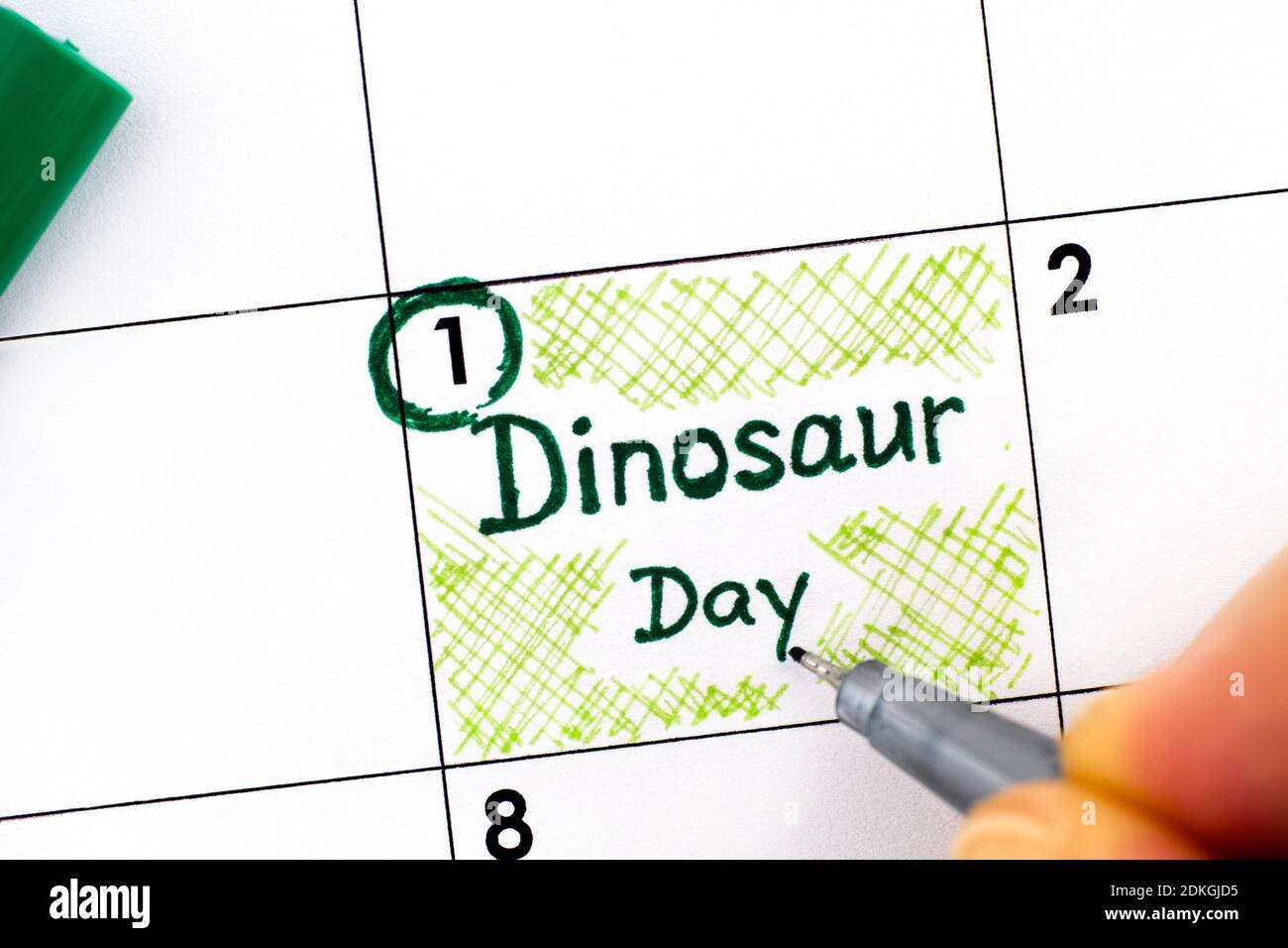 Woman fingers with pen writing reminder Dinosaur Day in calendar. June ...