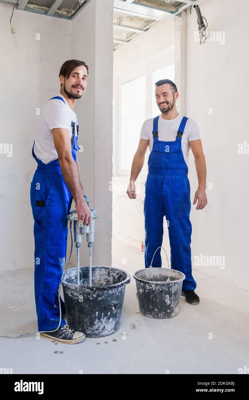 Two workers in blue uniform prepare cement in a bucket Stock Photo - Alamy