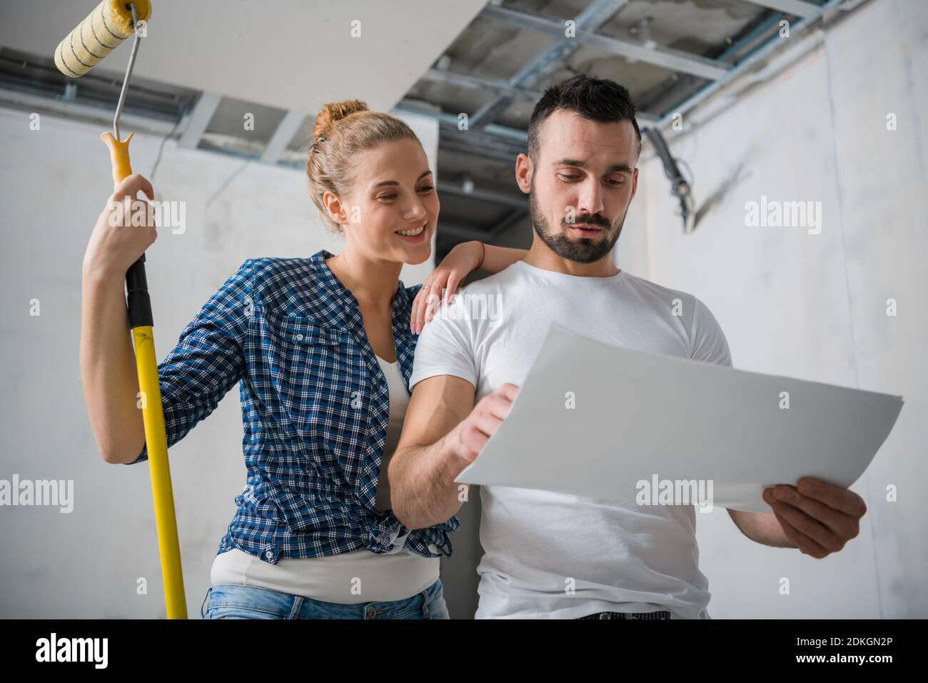 A woman holds a roller in her hand and hugs a workman. They look at the ...