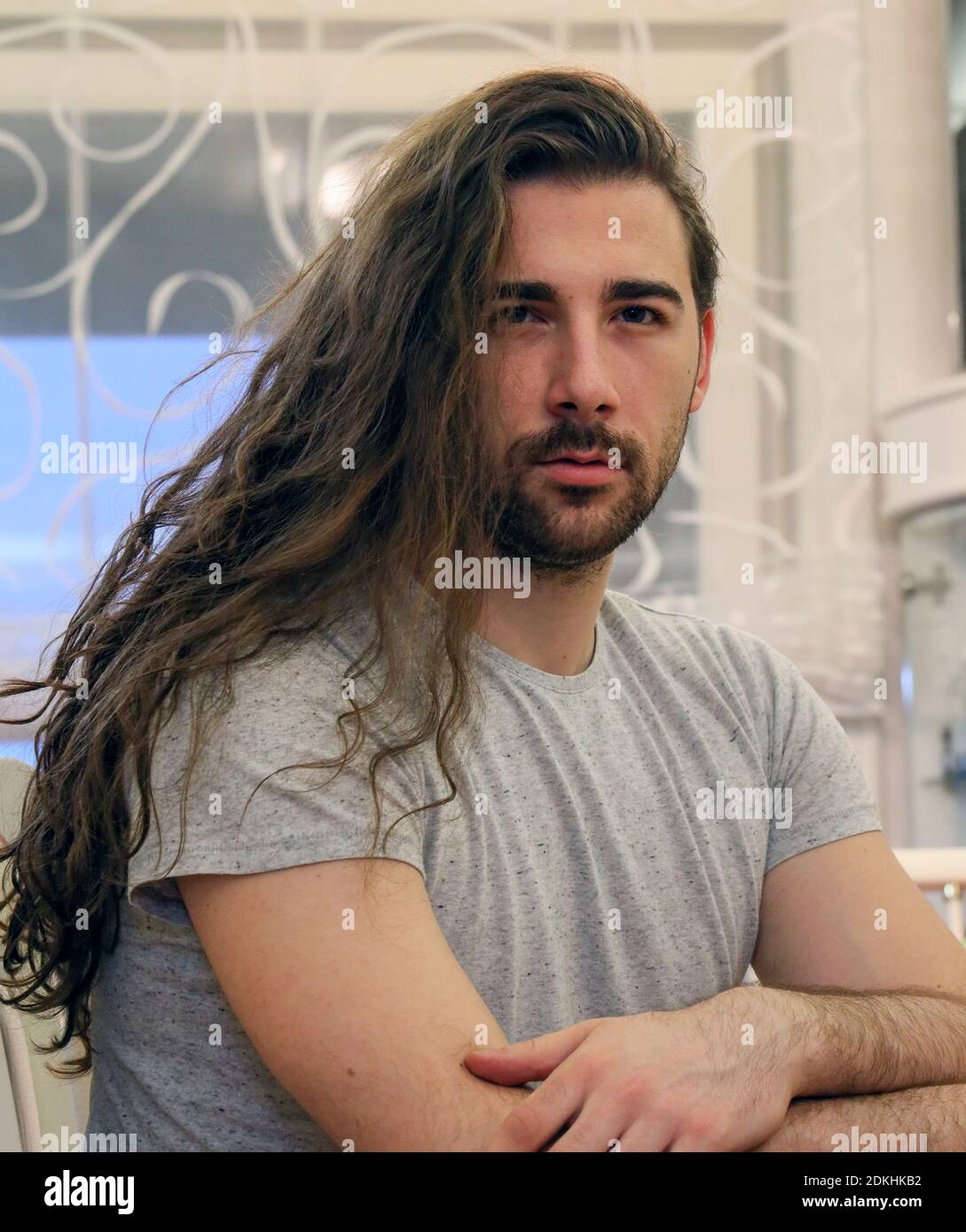 Attractive, young bearded male model with long hair posing indoors ...