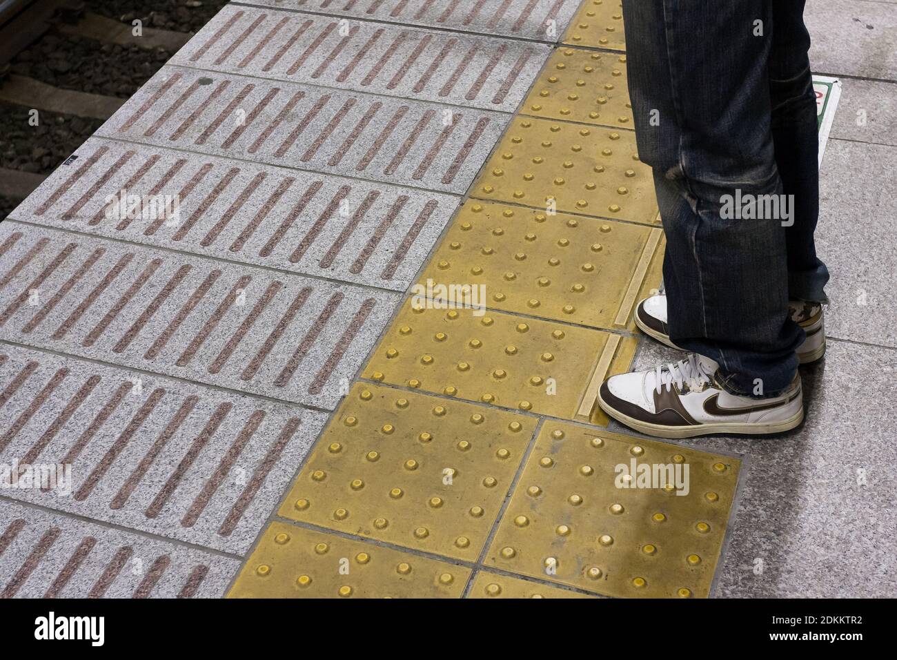 Legs of a passenger waiting behind a yellow safety line made of Tenji ...