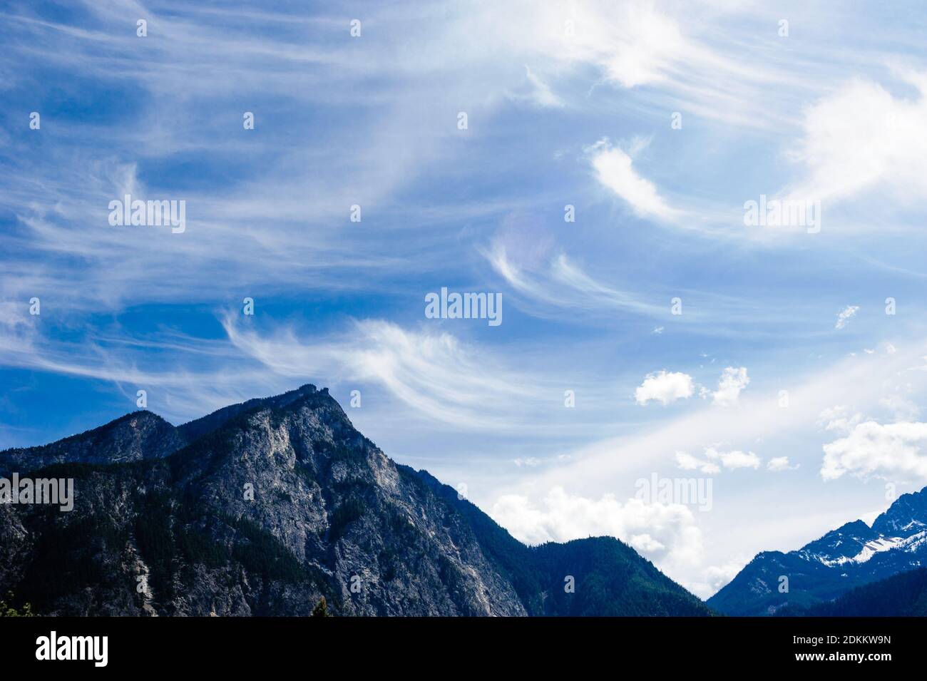 Cirrus clouds spreading into curved patterns above mountains in British ...
