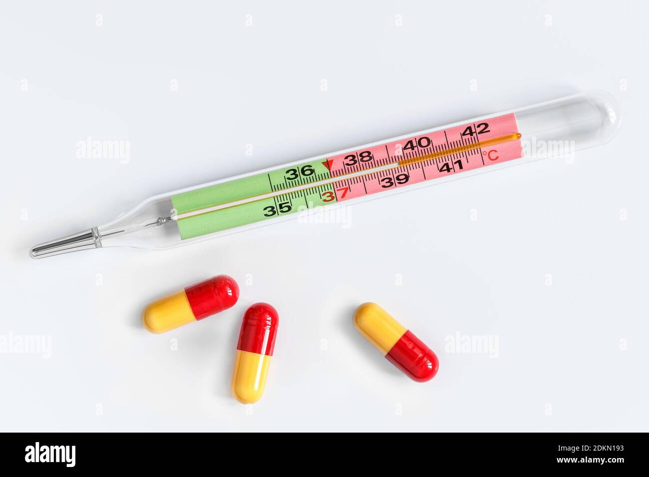 Mercury thermometer and three yellow-red capsules with medicine on a ...