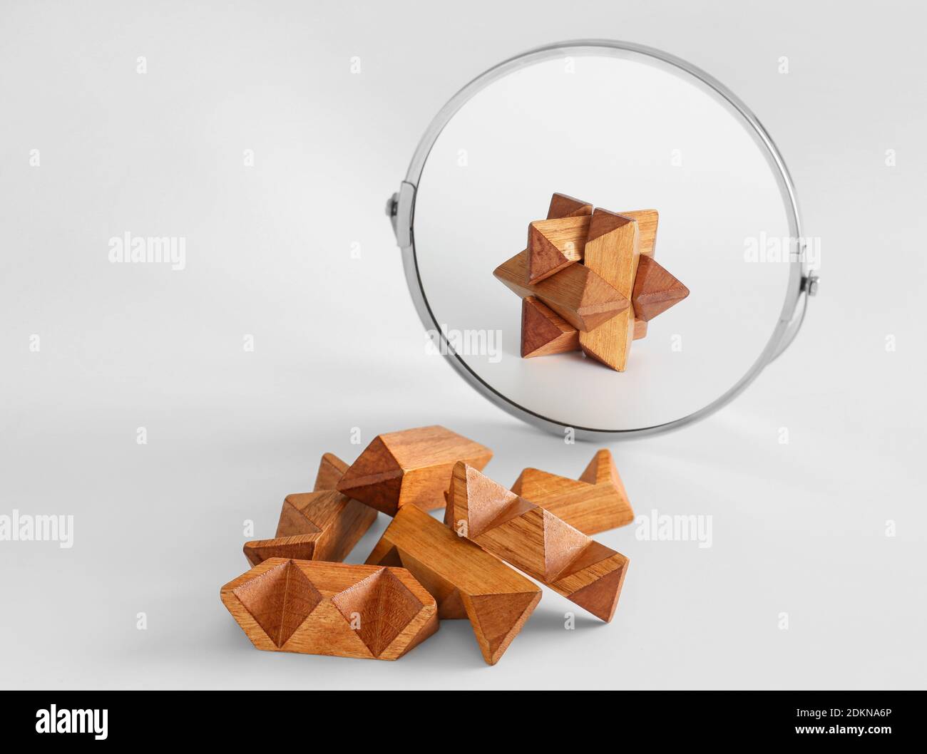 Wooden puzzle looking at its reflection in mirror on light background ...