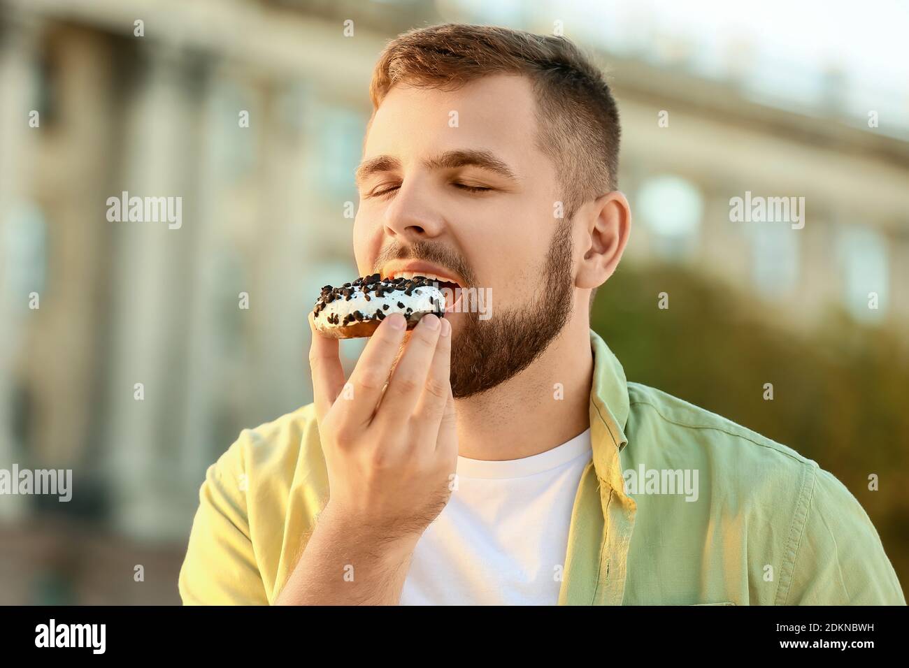 Handsome young man eating sweet donut outdoors Stock Photo - Alamy