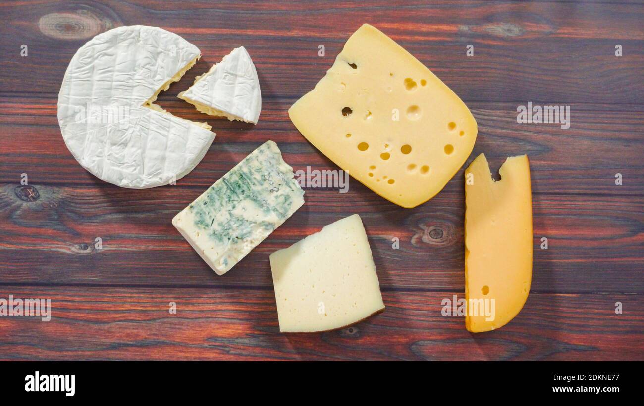Flat lay. Large wedges of gourmet cheese on a rustic wood background ...