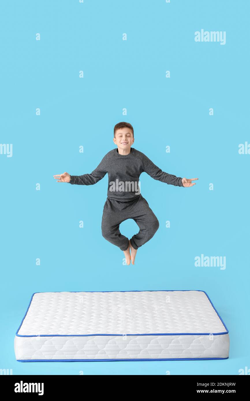 Meditating little boy jumping on mattress against color background ...