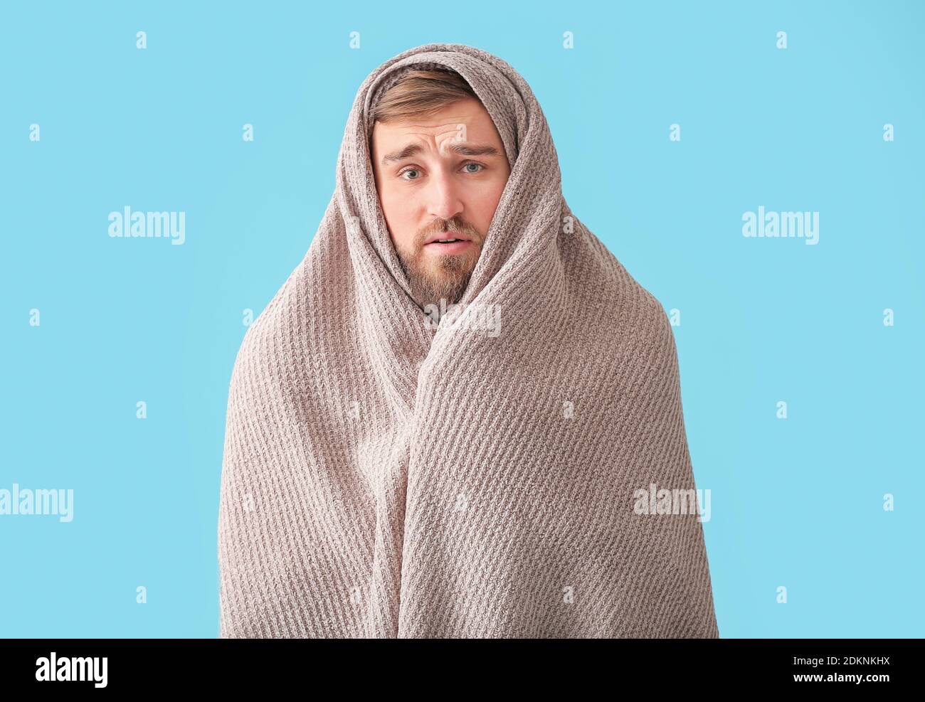 Freezing young man wrapped in warm plaid on color background. Concept ...