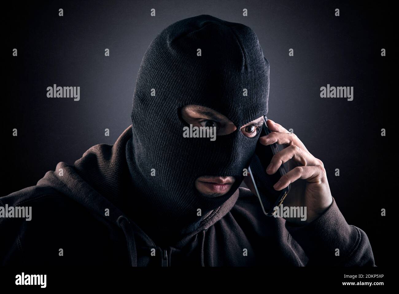 Criminal wearing black balaclava and hoodie with a smartphone in the ...