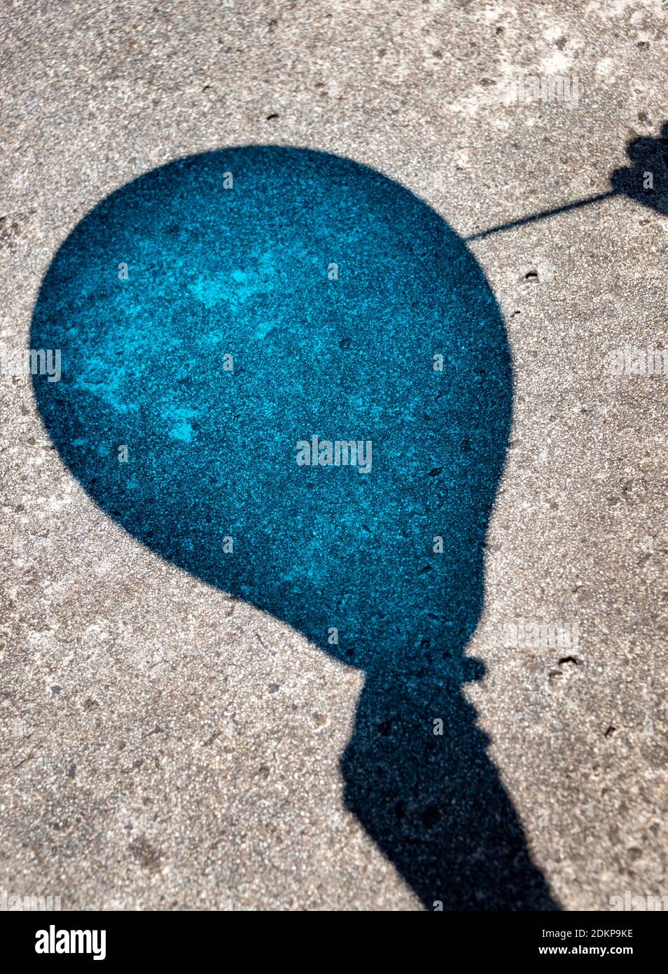 the glowing shadow of a blue balloon against grey pavement, with a ...