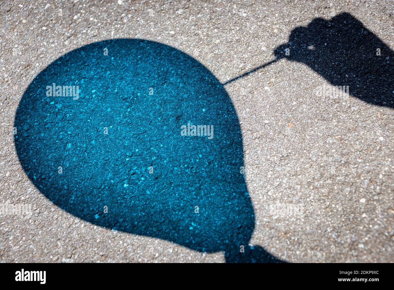 the glowing shadow of a blue balloon against grey pavement, with a ...