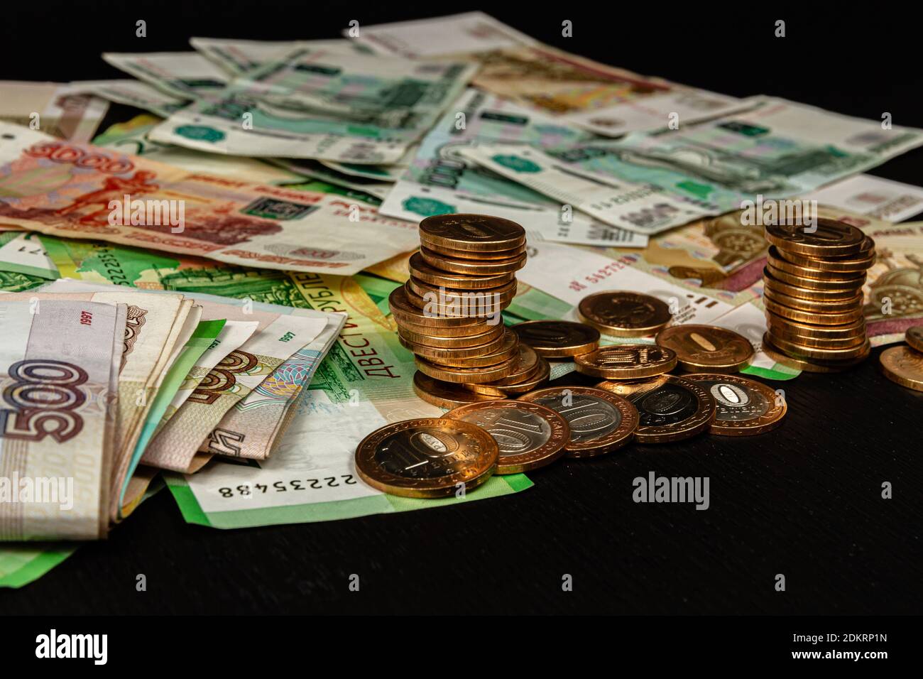 stack of metallic gold coins and paper money lie on a black wooden ...
