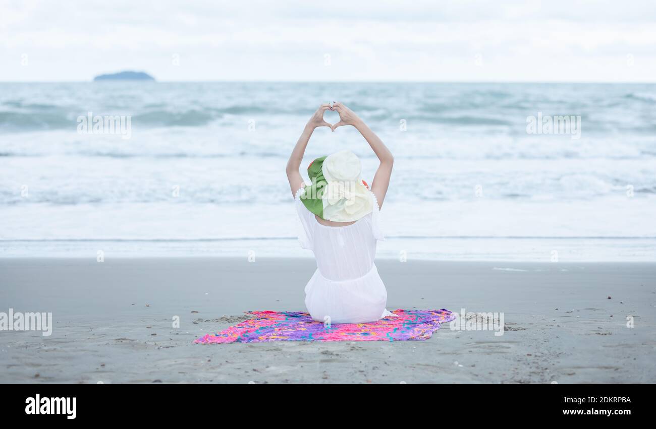 Rear View Of Woman Making Heart Shape While Sitting At Beach Stock ...