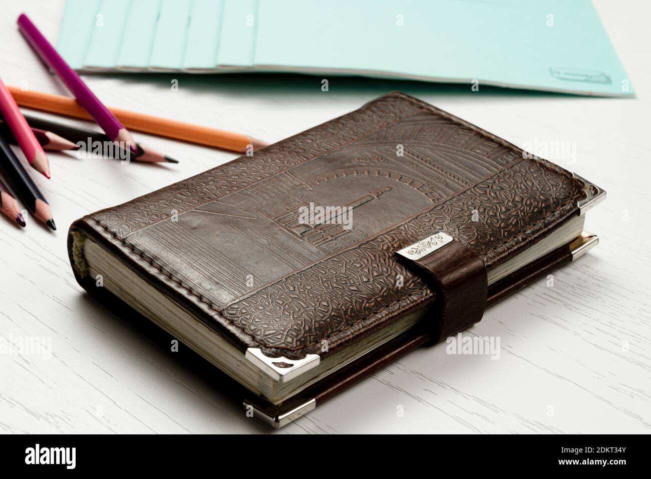 colored pencils and brown leather diary lie on a white wooden table ...