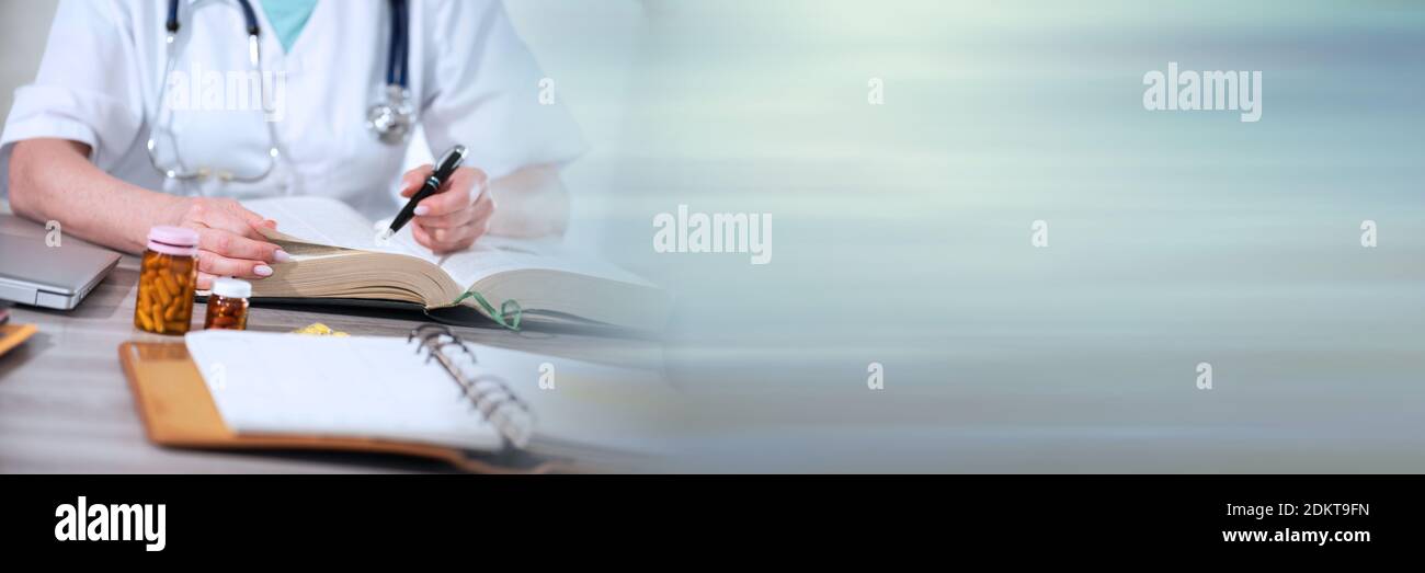 Female doctor reading a textbook in medical office; panoramic banner ...