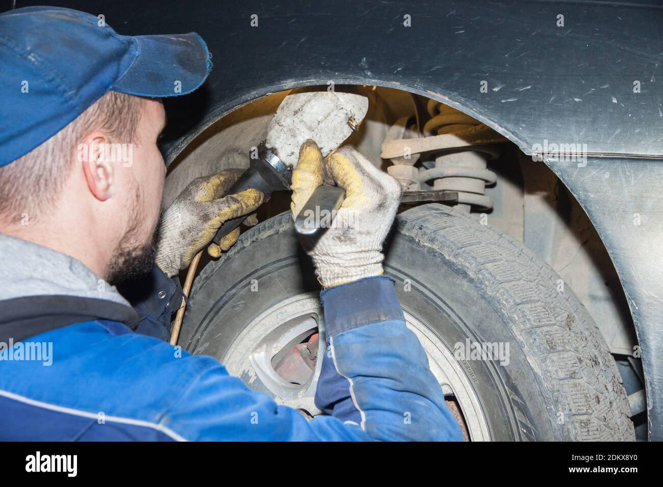 A mechanic with a flashlight and a crowbar examines the front ...