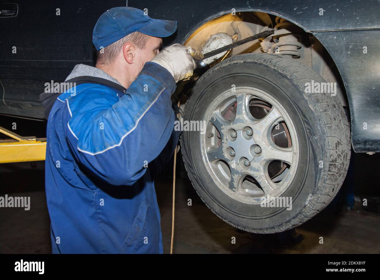 A mechanic with a flashlight and a crowbar examines the front ...