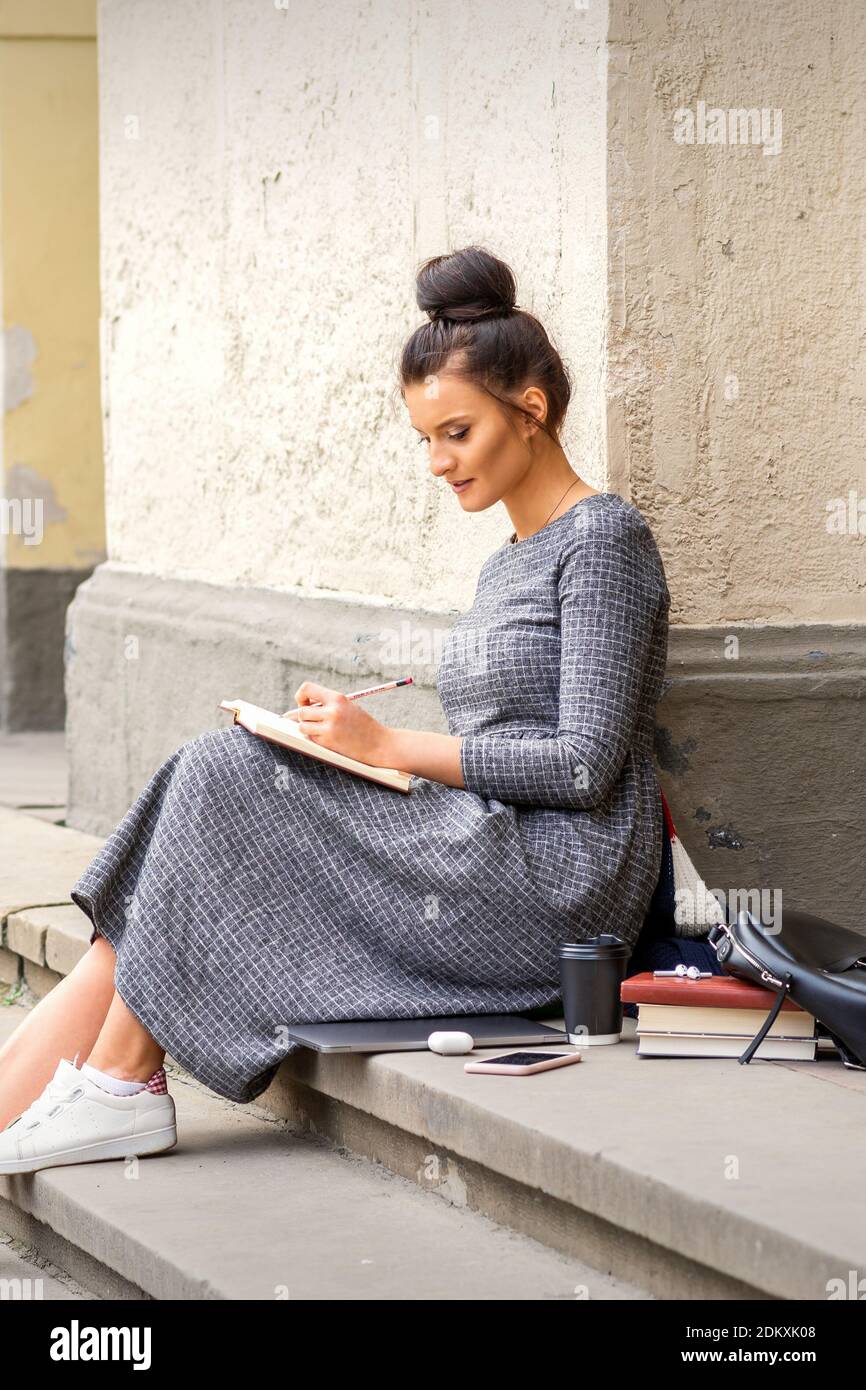 Female student in long dress reading a book on stairs of university ...