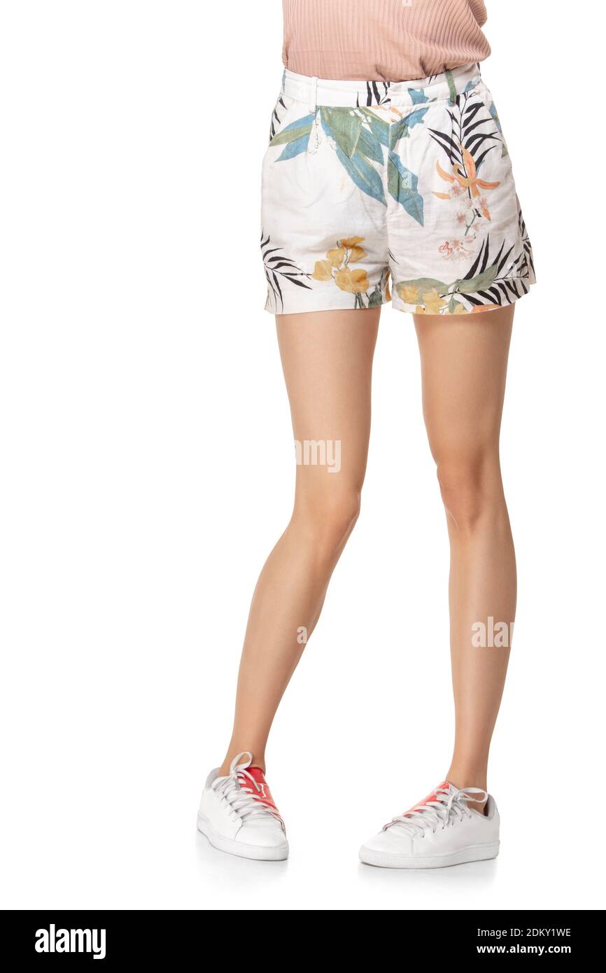 Slender female legs in shorts and sneakers isolated on white background ...
