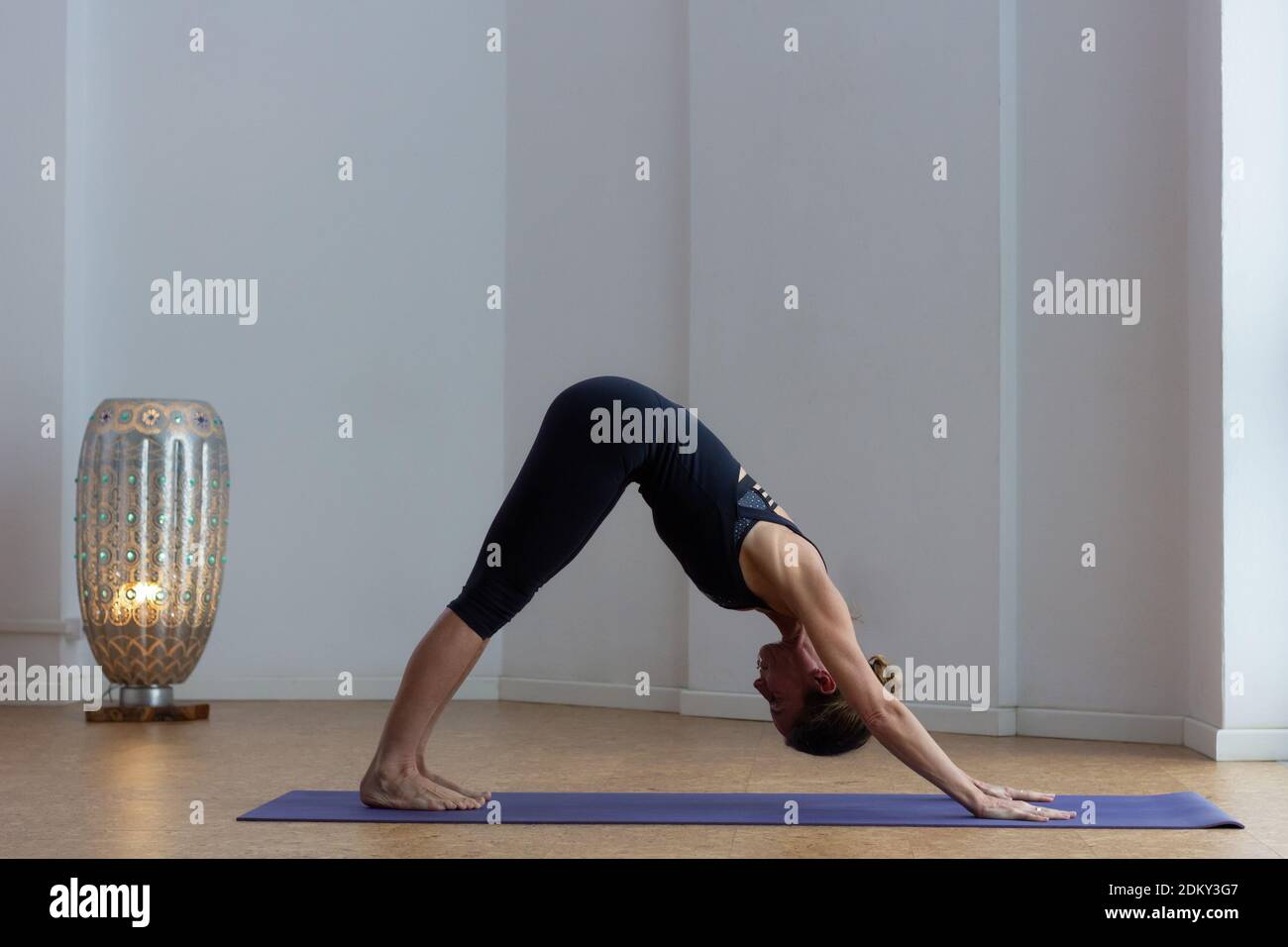 Slim woman doing adho mukha svanasana yoga pose in studio. Female yogi in downward facing dog ...
