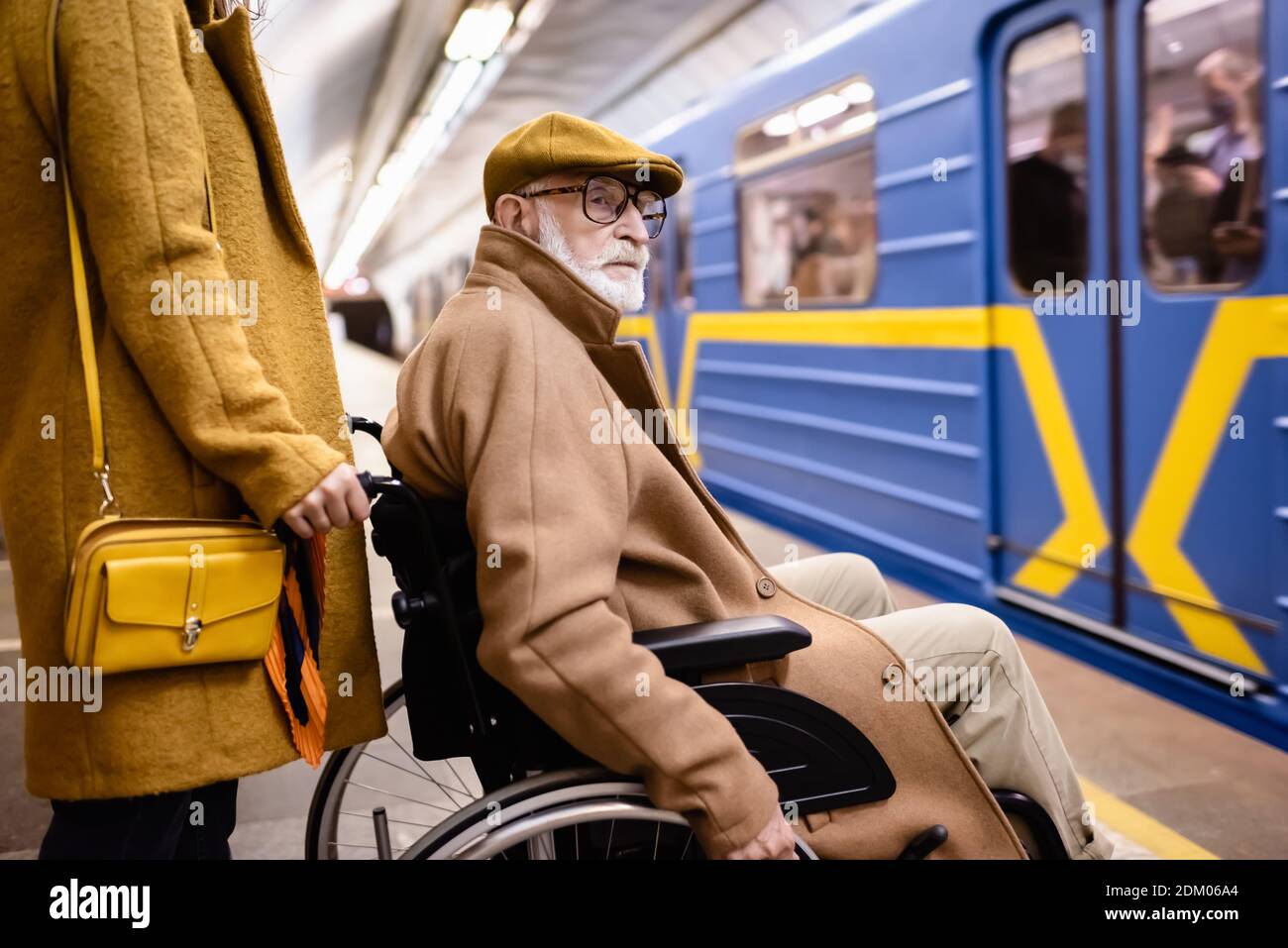 woman holding wheelchair of aged disabled man on underground platform ...
