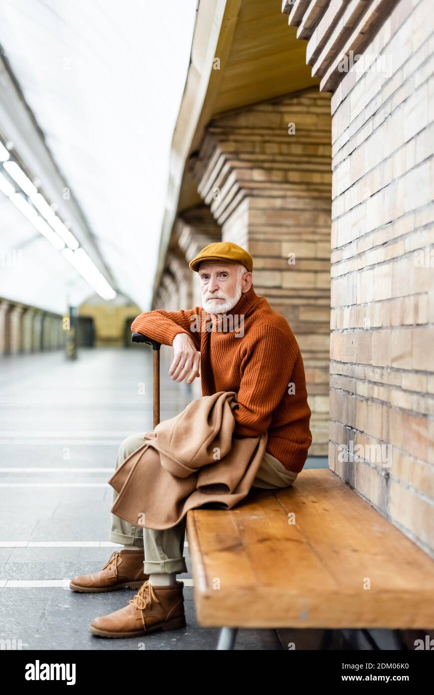 aged man in autumn outfit leaning on walking stick while sitting on ...