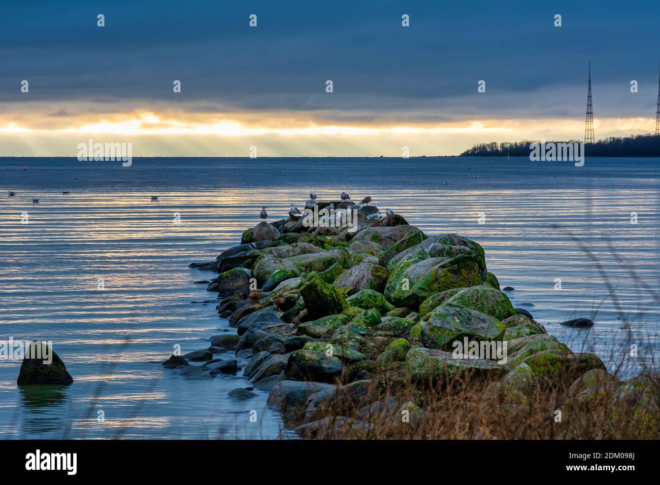 A beautiful sunset over the green boulders on a wave breaker. Photo ...