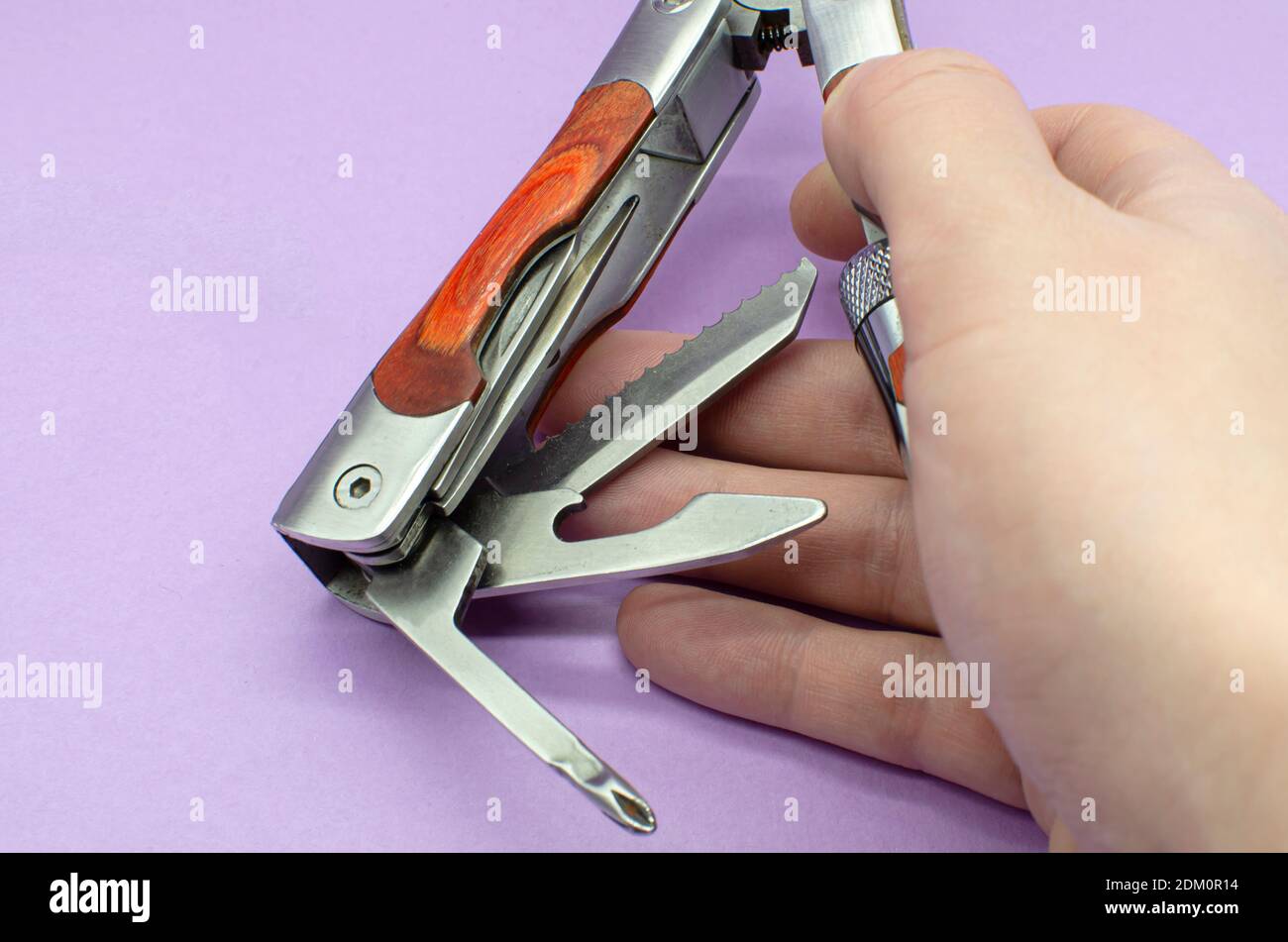 multitool turned into pliers, knife, screwdriver in the hand on violet ...