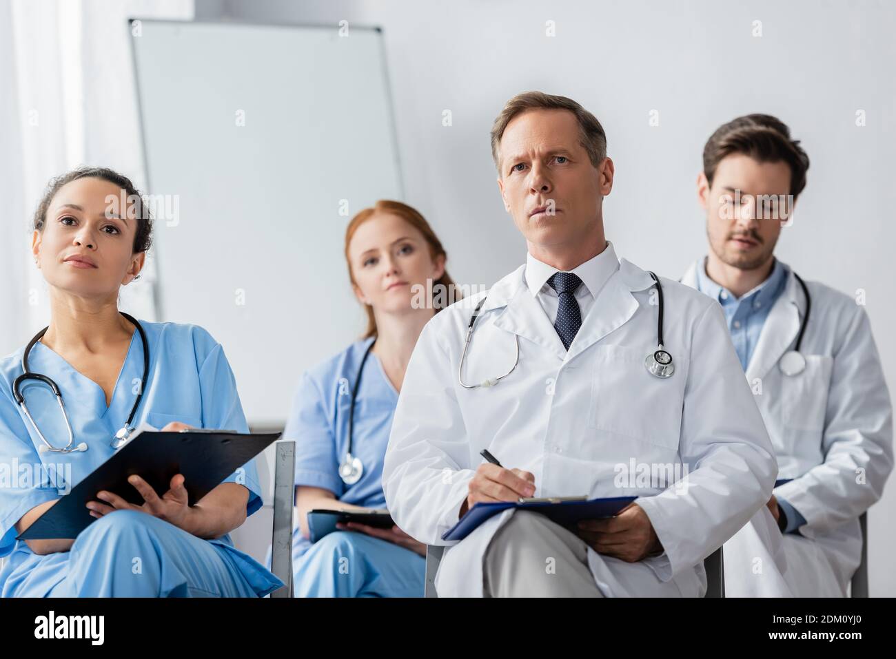 Focused multicultural nurses and doctors with clipboards looking away ...