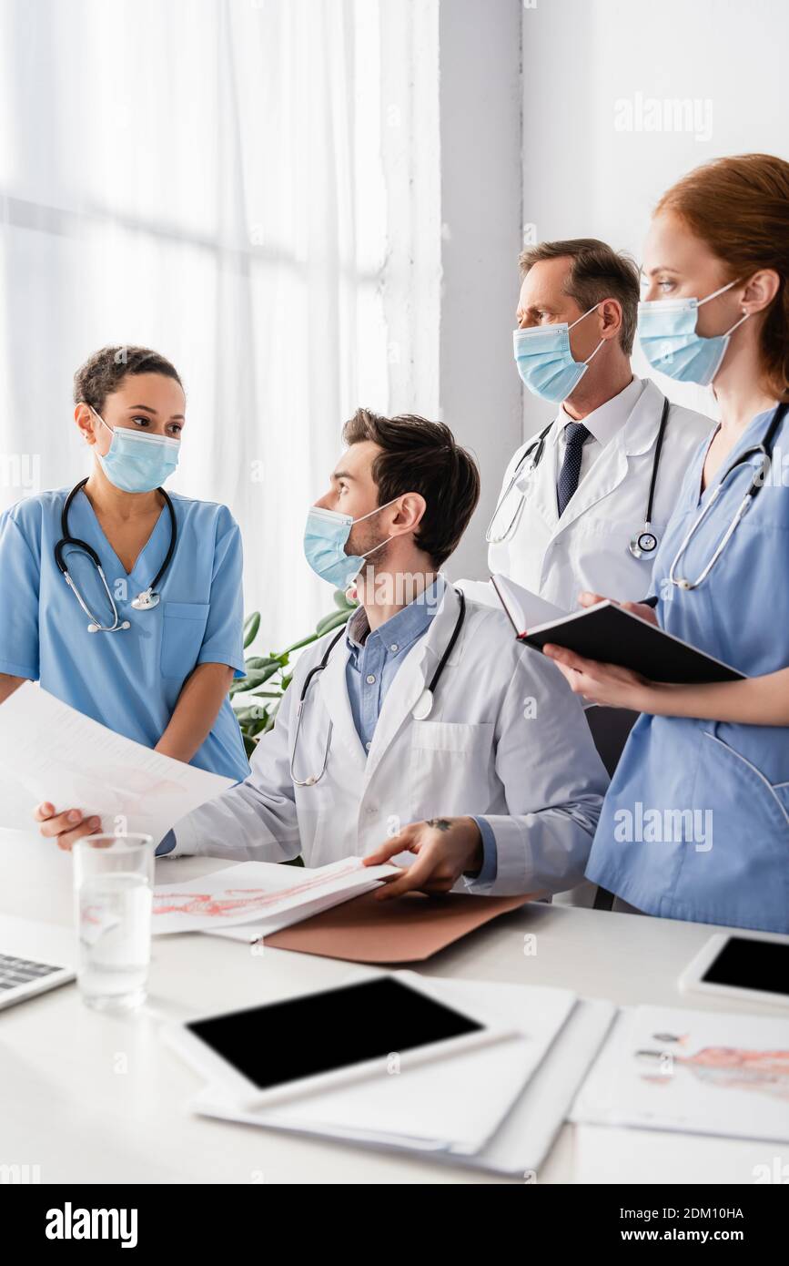 Hospital staff in medical masks looking at african american nurse ...