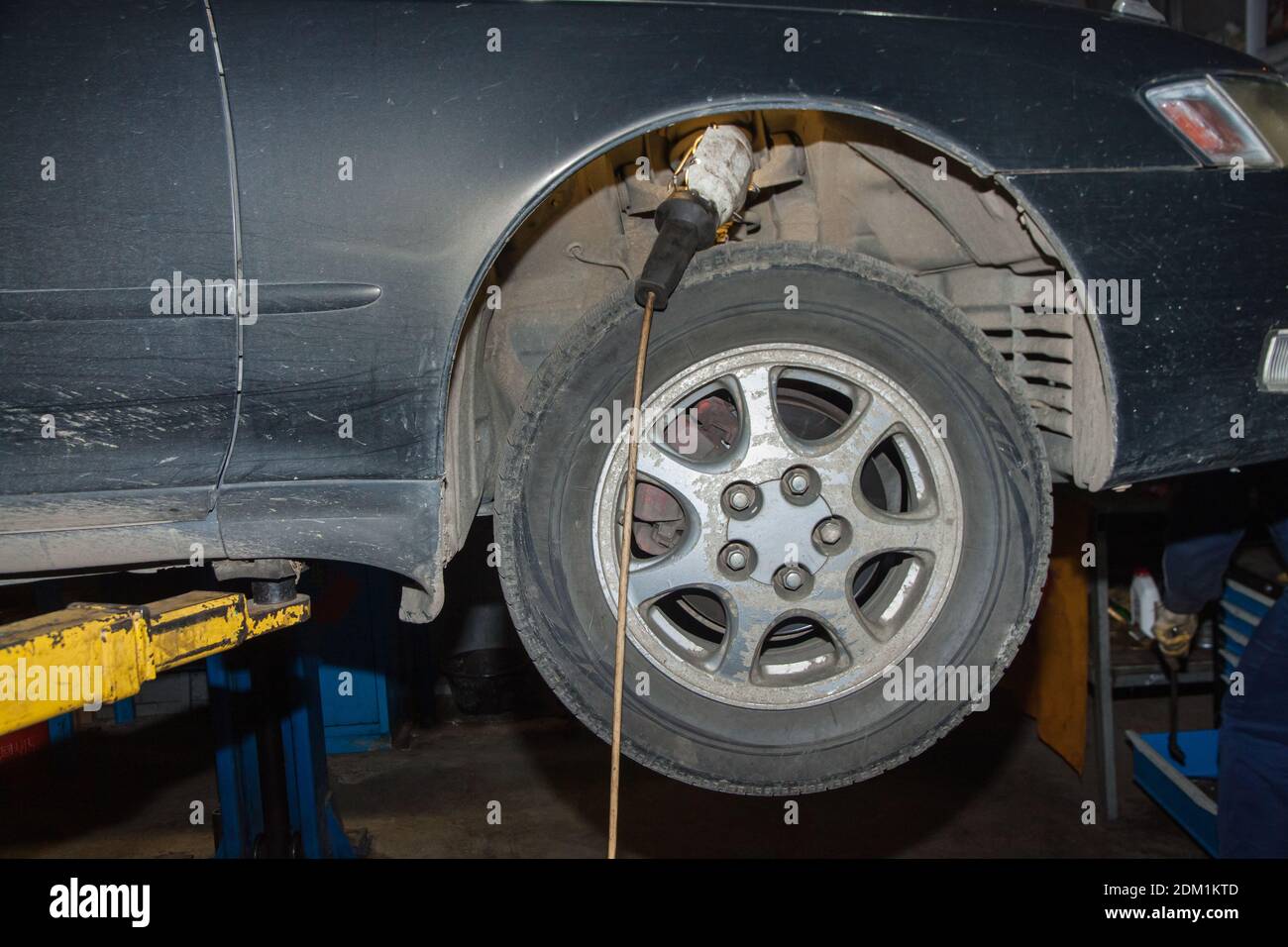 The car is hanging on a hydraulic lift in an auto repair shop. Above ...