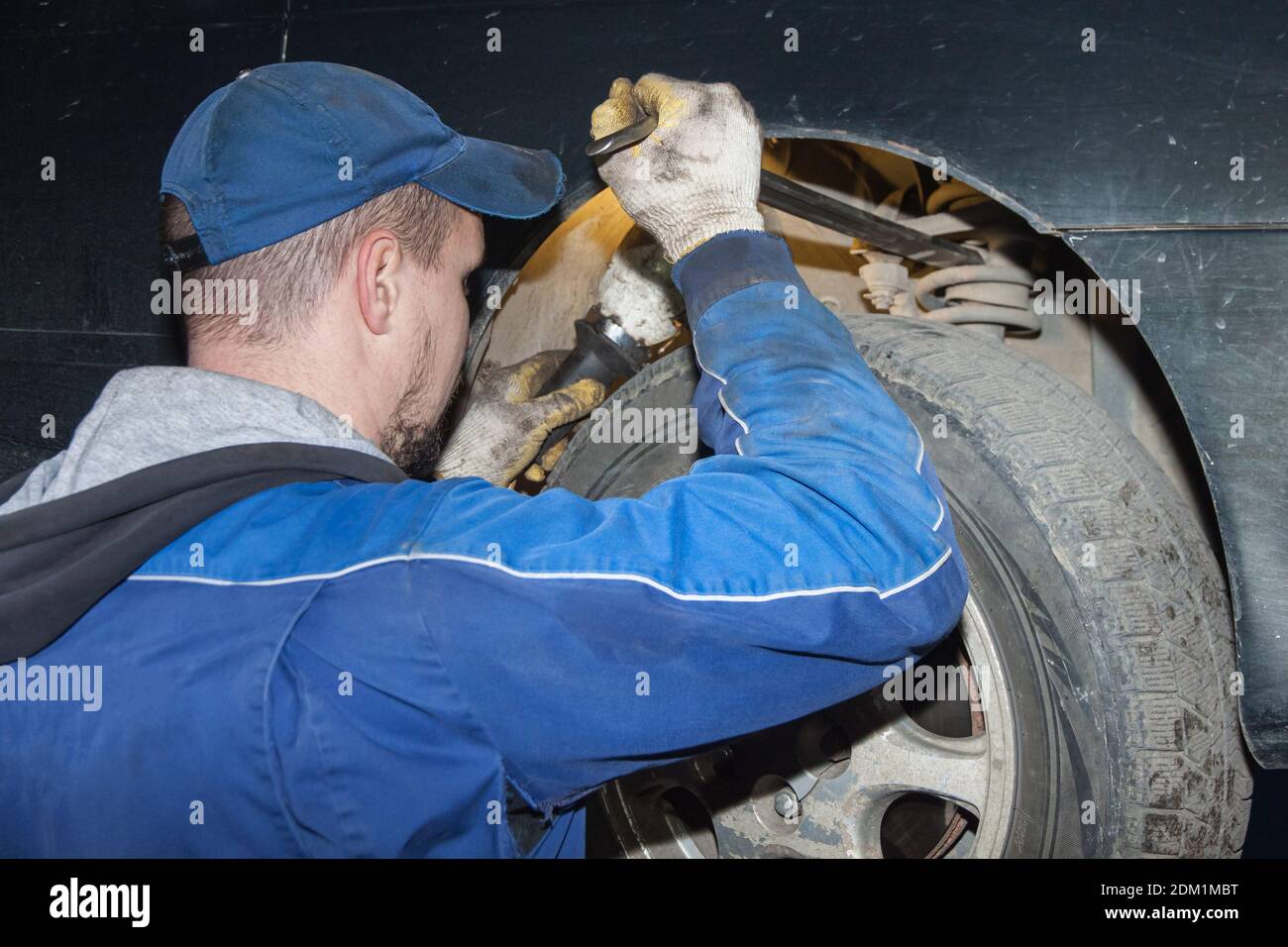 A mechanic with a flashlight and a crowbar examines the front ...