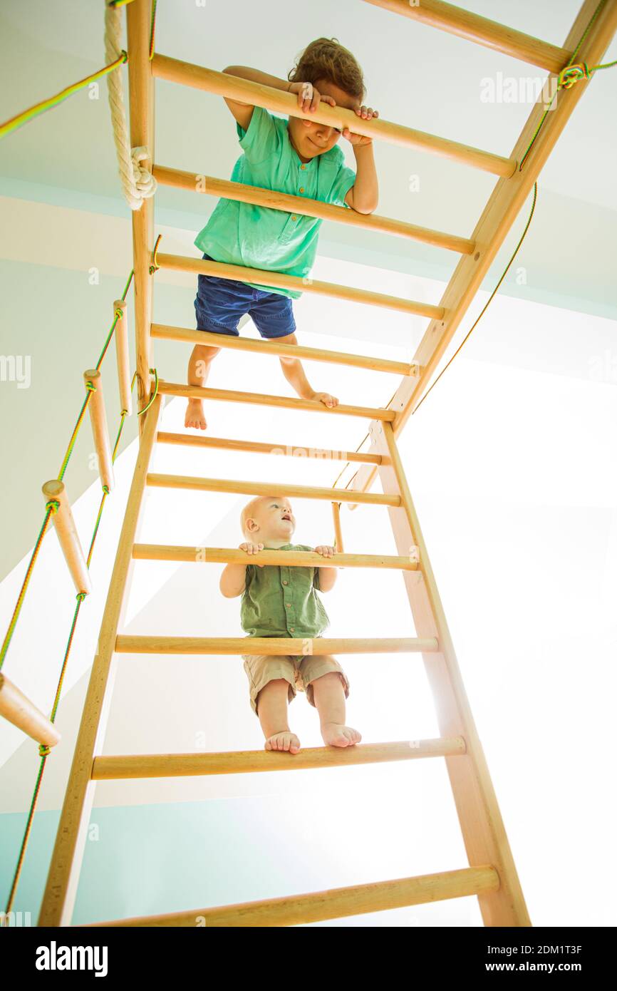 Small boy copying elder brother, following him on wall bars Stock Photo ...