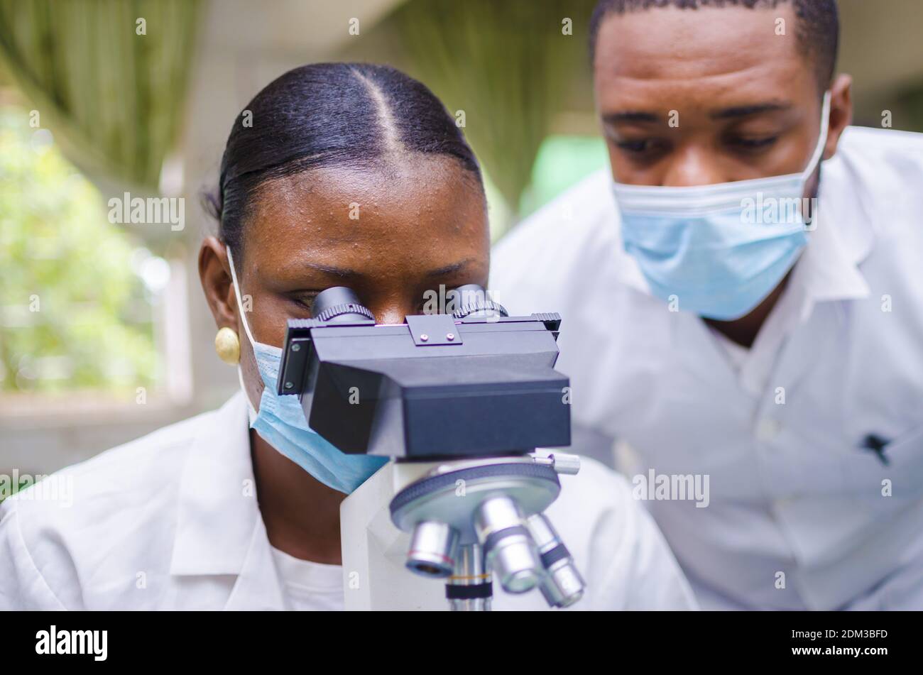 A young African male and female scientists looking through a microscope ...