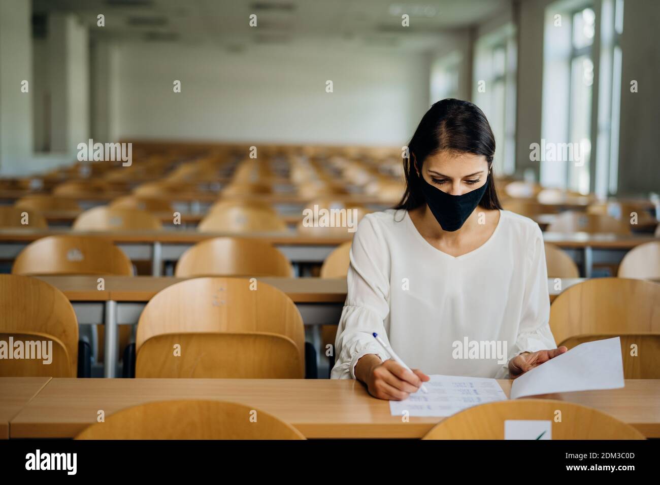 Female student taking an exam wearing a protective face mask in an ...