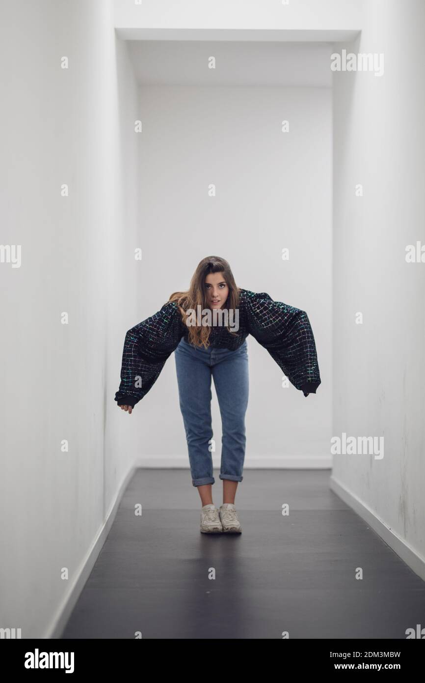 Portrait Of Young Woman Bending In Corridor Against Wall Stock Photo ...
