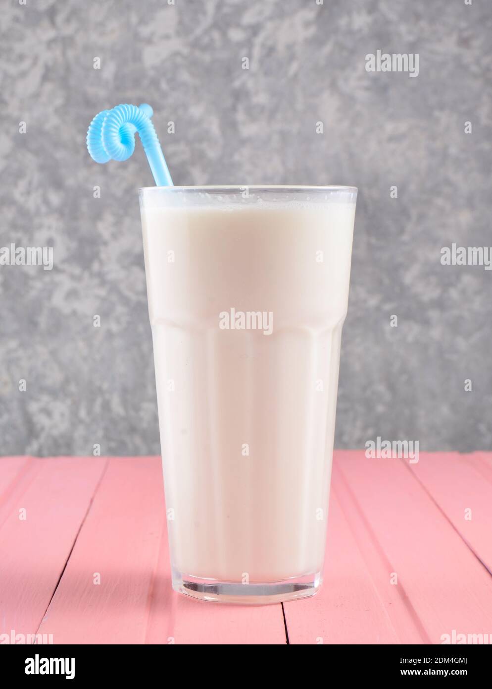 A glass of milkshake with a straw on a pastel color wooden table on the ...