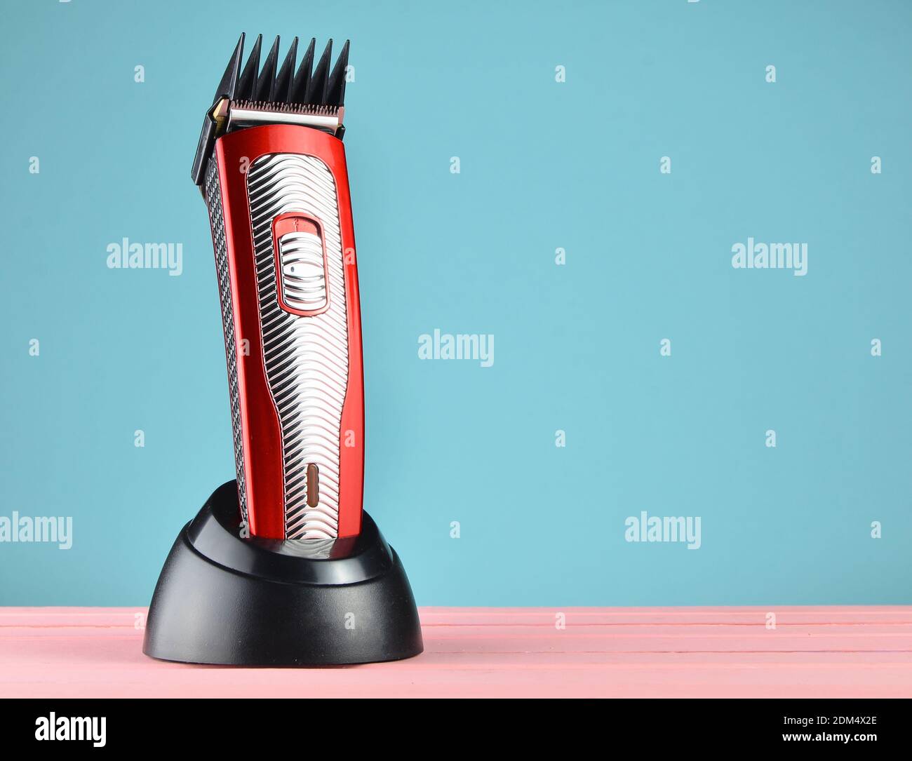 Wireless clipper with a nozzle stands on a charging station on a pastel ...